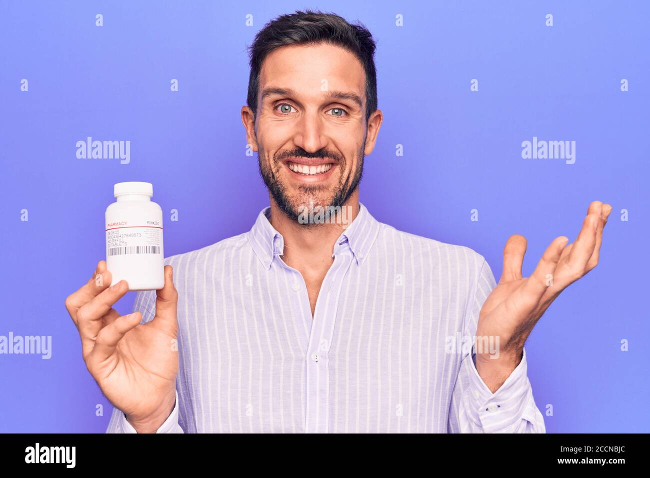 Young handsome man holding jar of medicine pills standing over isolated ...