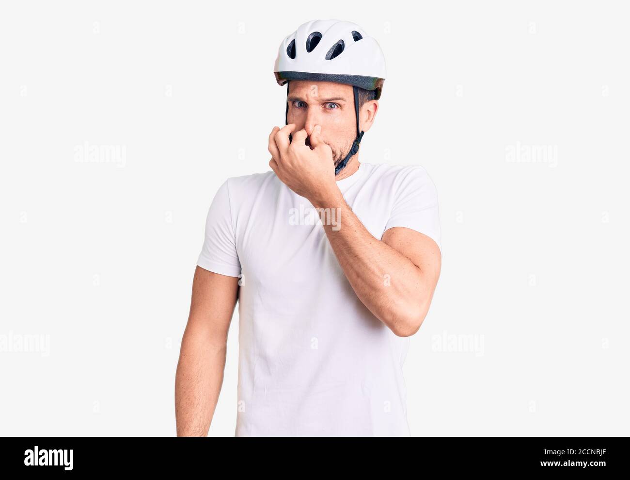 Young handsome man wearing bike helmet smelling something stinky and ...
