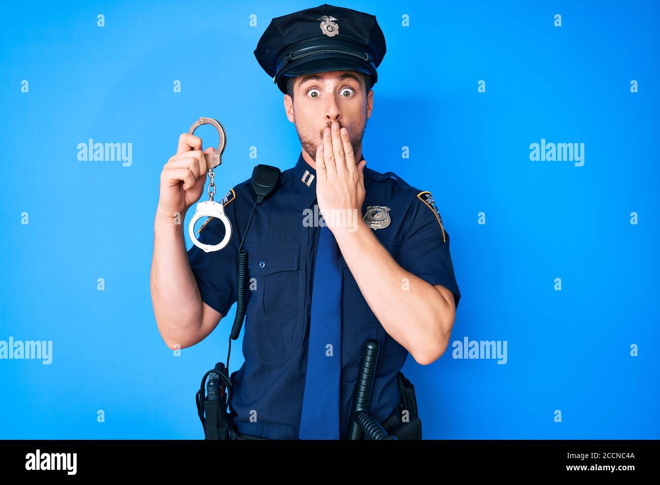 Young caucasian man wearing police uniform holding handcuffs covering ...