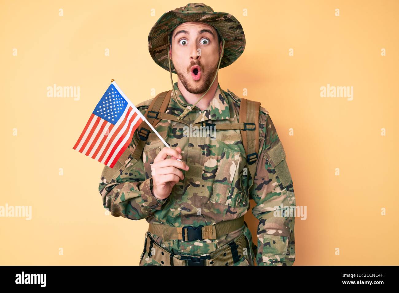 Young caucasian man wearing camouflage army uniform holding usa flag ...
