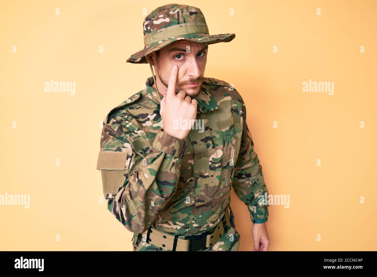 Young caucasian man wearing camouflage army uniform pointing to the eye ...