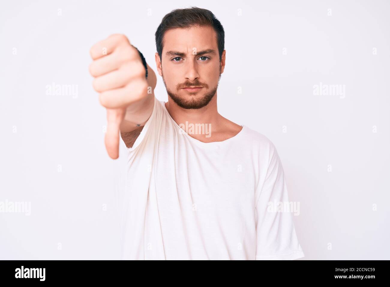 Young handsome man wearing casual white tshirt looking unhappy and ...