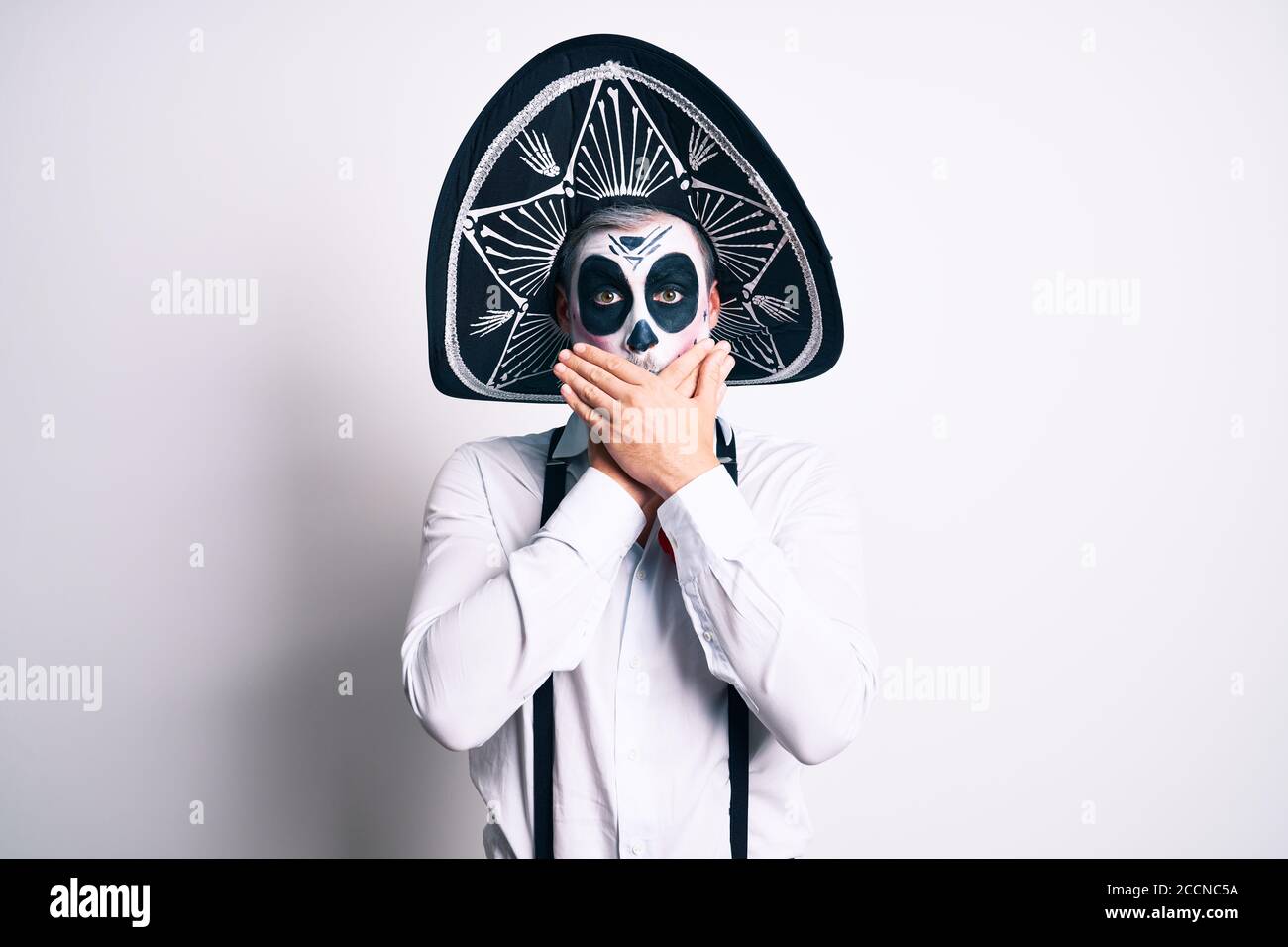 Man wearing day of the dead costume over white shocked covering mouth ...