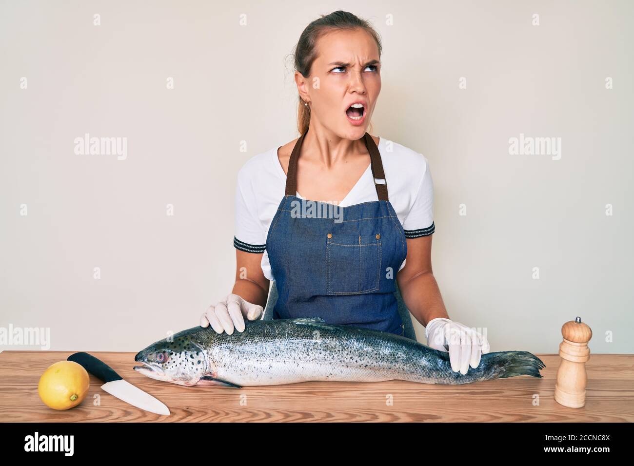 Beautiful caucasian woman fishmonger selling fresh raw salmon angry and ...