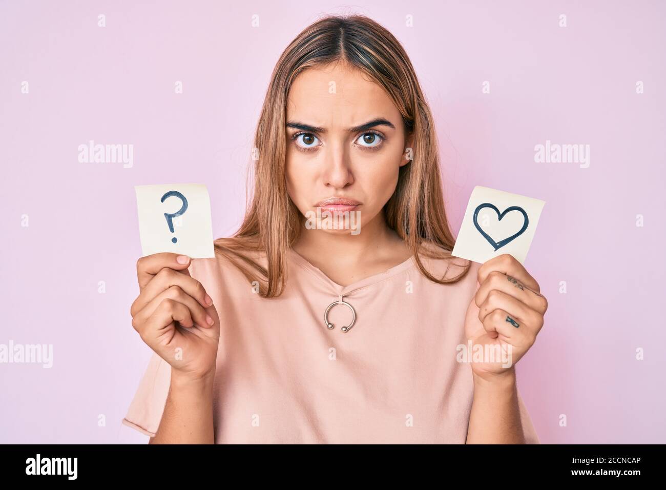 Young beautiful blonde woman holding heart and question mark reminder ...