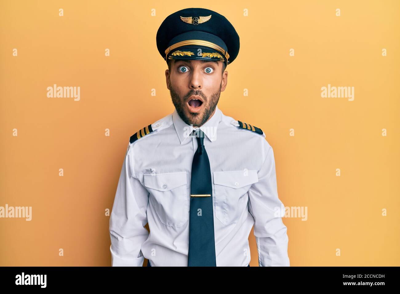 Handsome hispanic man wearing airplane pilot uniform afraid and shocked ...