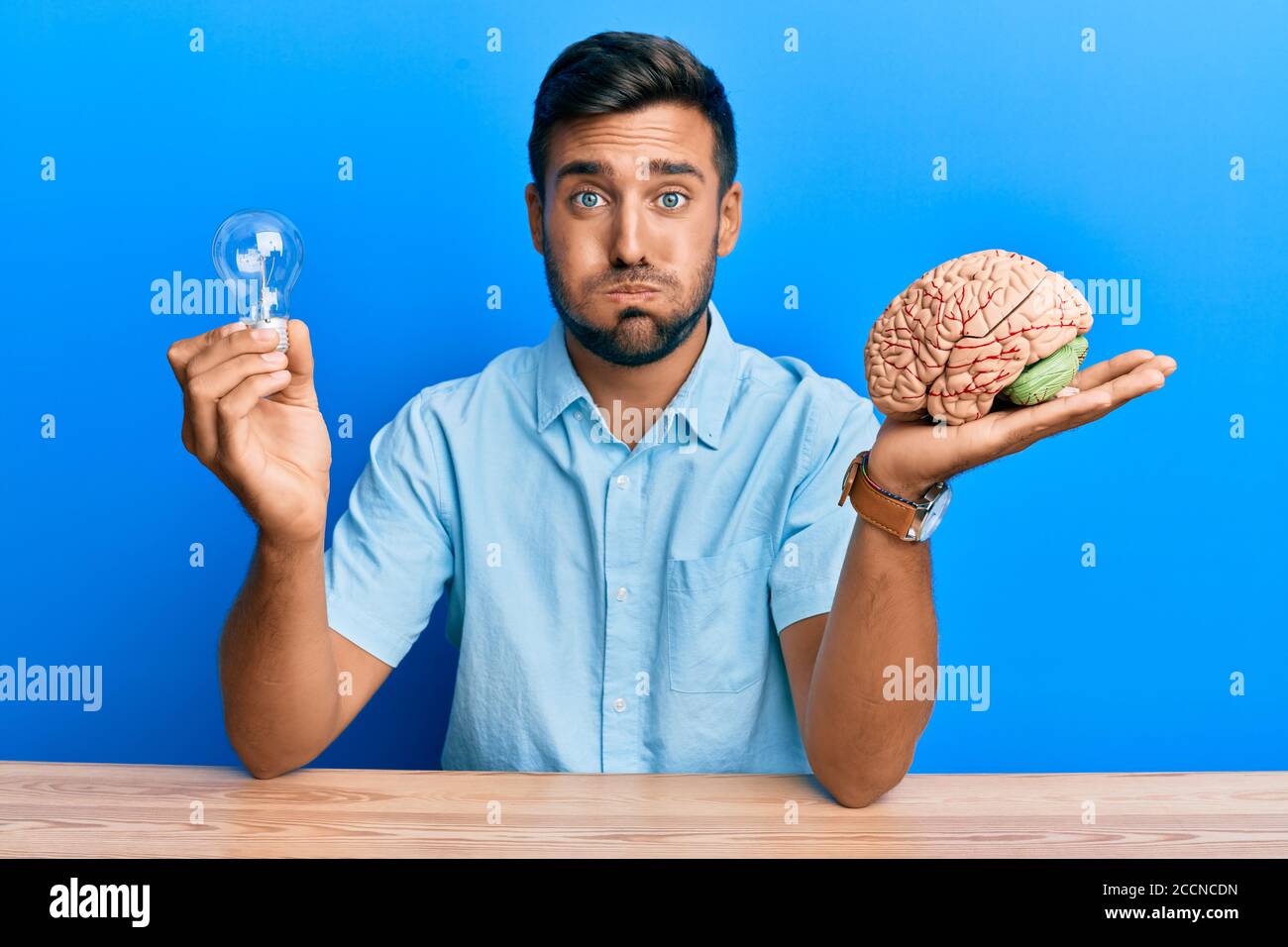 Handsome hispanic man holding lightbulb and brain for inspiration and ...