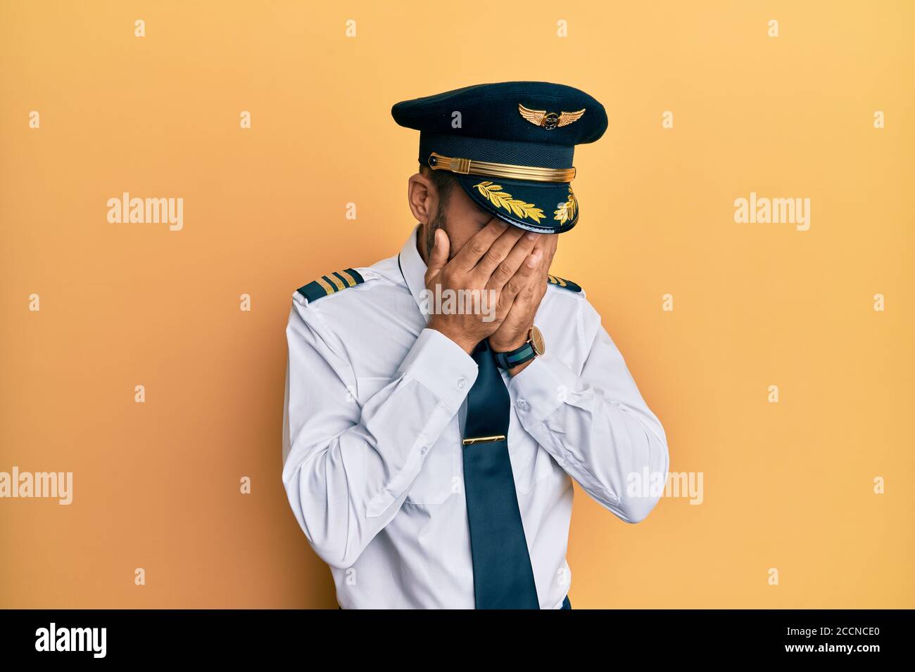 Handsome hispanic man wearing airplane pilot uniform with sad ...