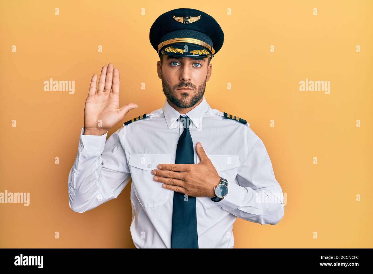 Handsome hispanic man wearing airplane pilot uniform swearing with hand ...