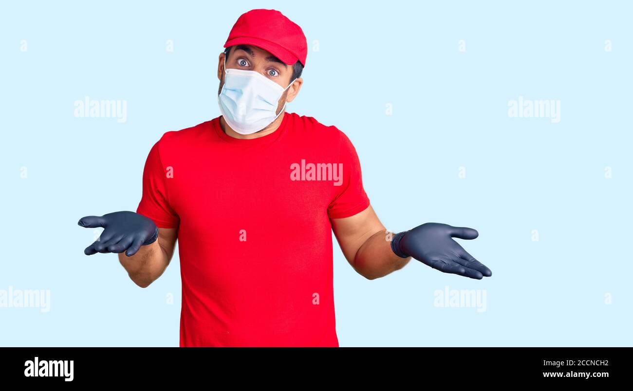 Young hispanic man wearing covid-19 safety mask clueless and confused ...