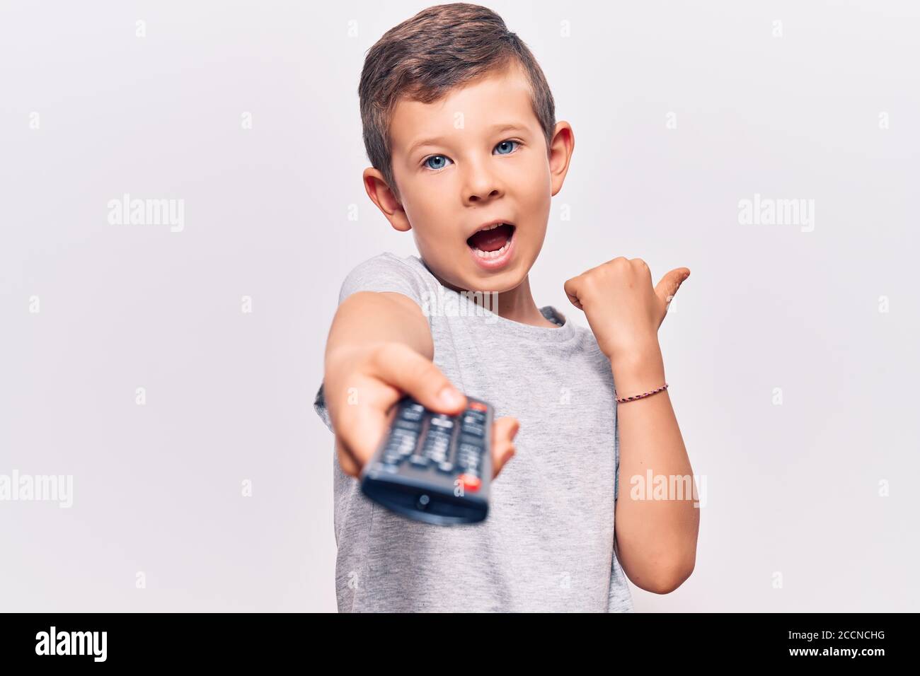 Cute blond kid holding television remote control pointing thumb up to ...