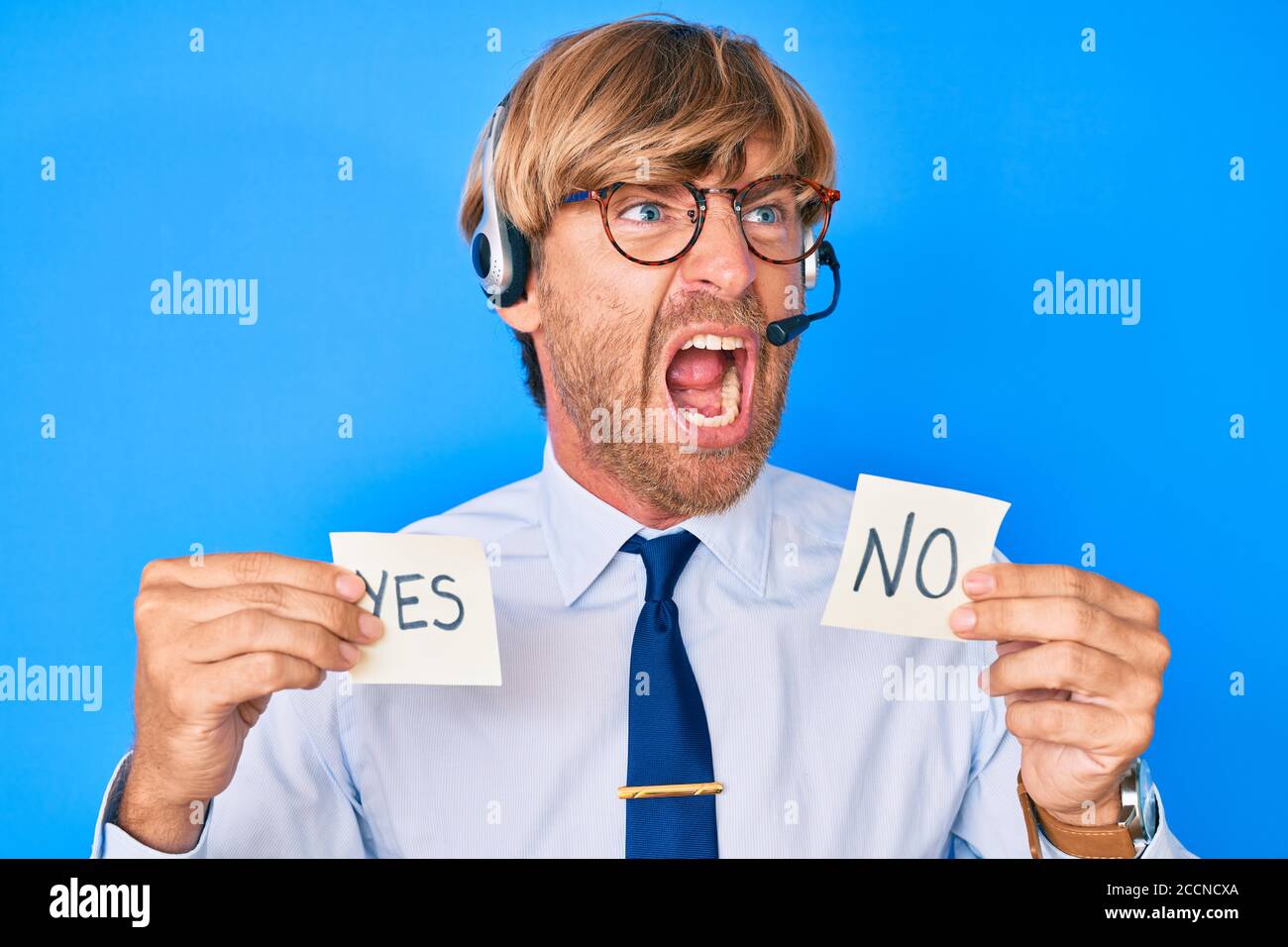 Young blond man wearing operator headset holding yes and no reminder ...