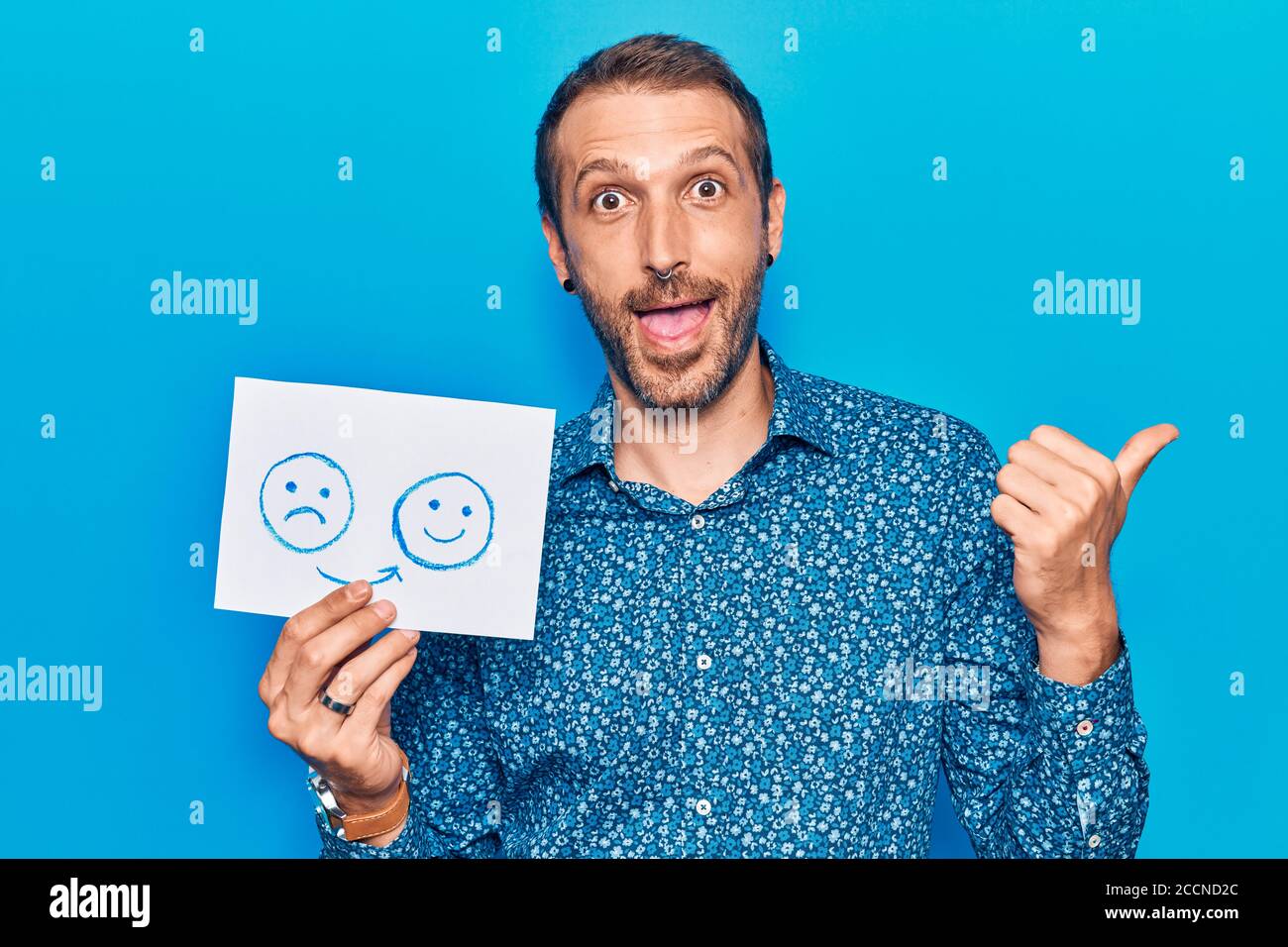 Young handsome man holding sad to happy emotion paper pointing thumb up ...