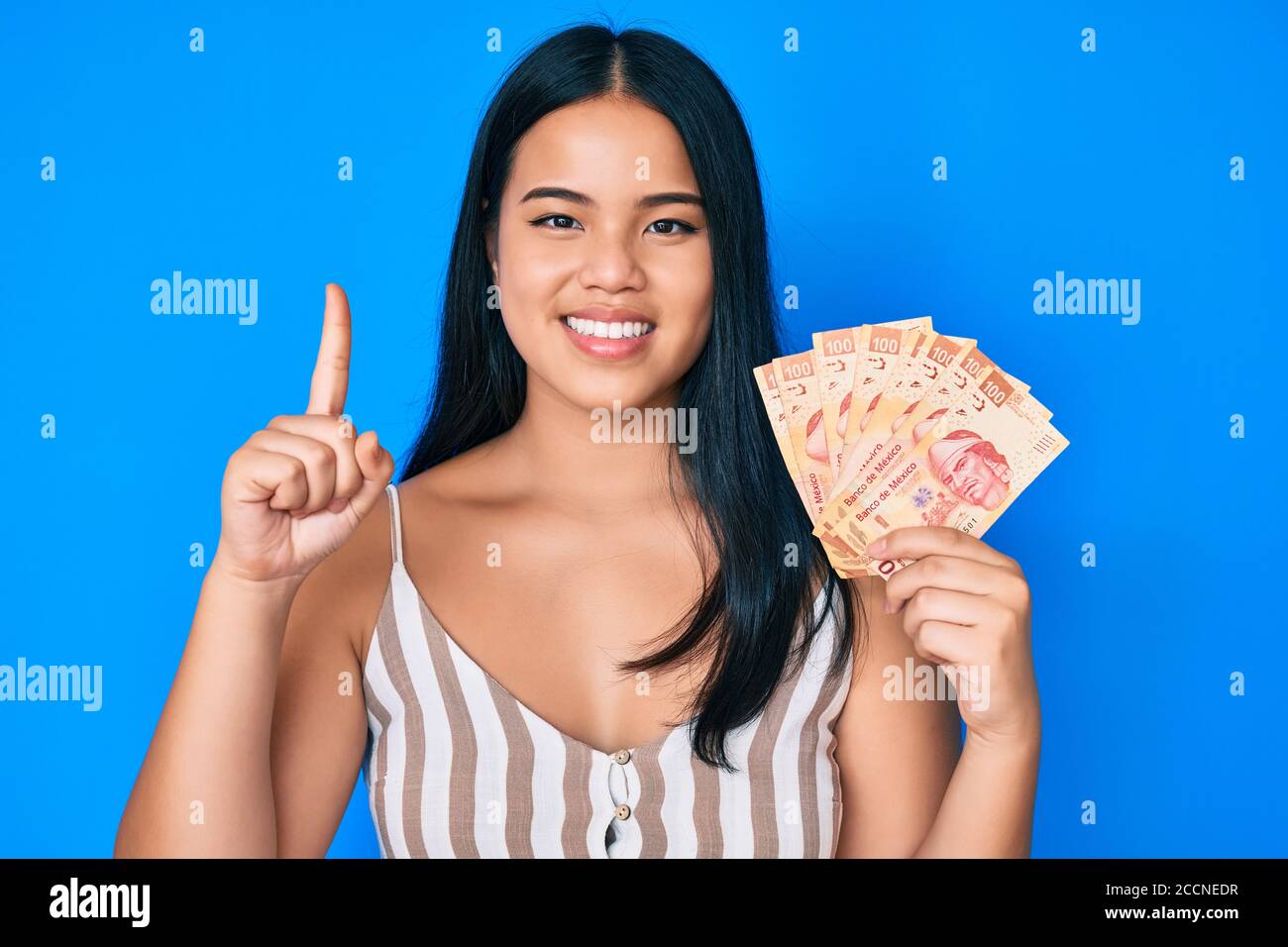 Young beautiful asian girl holding mexican pesos smiling with an idea ...