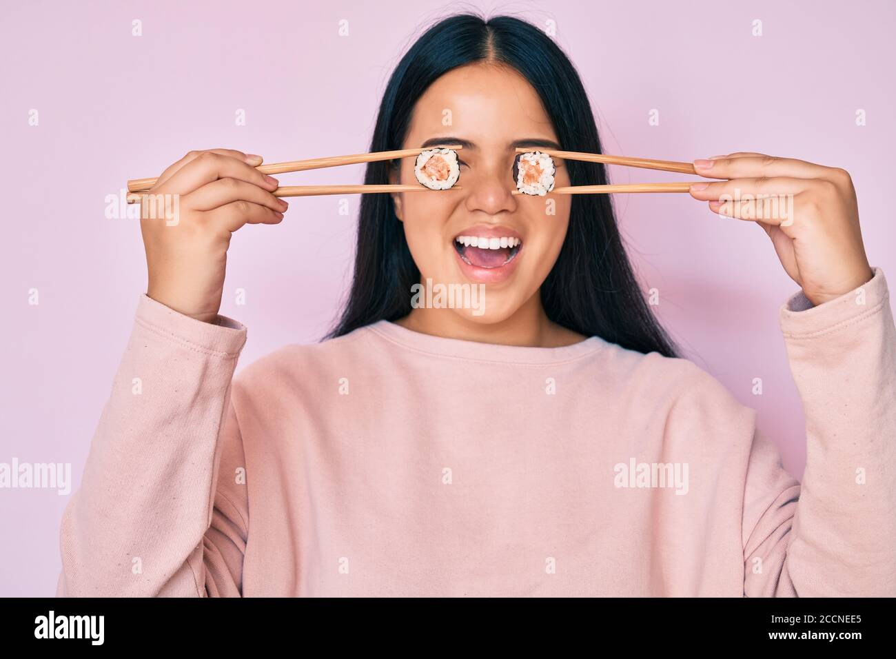 Young beautiful asian girl puting sushi on eyes using chopsticks ...
