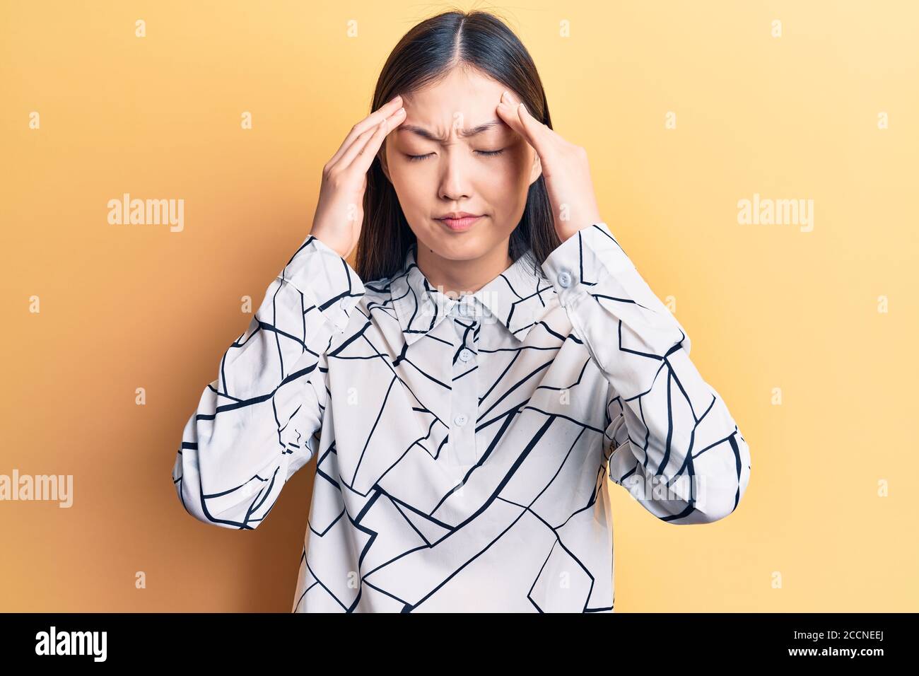 Young beautiful chinese woman wearing elegant shirt with hand on head ...