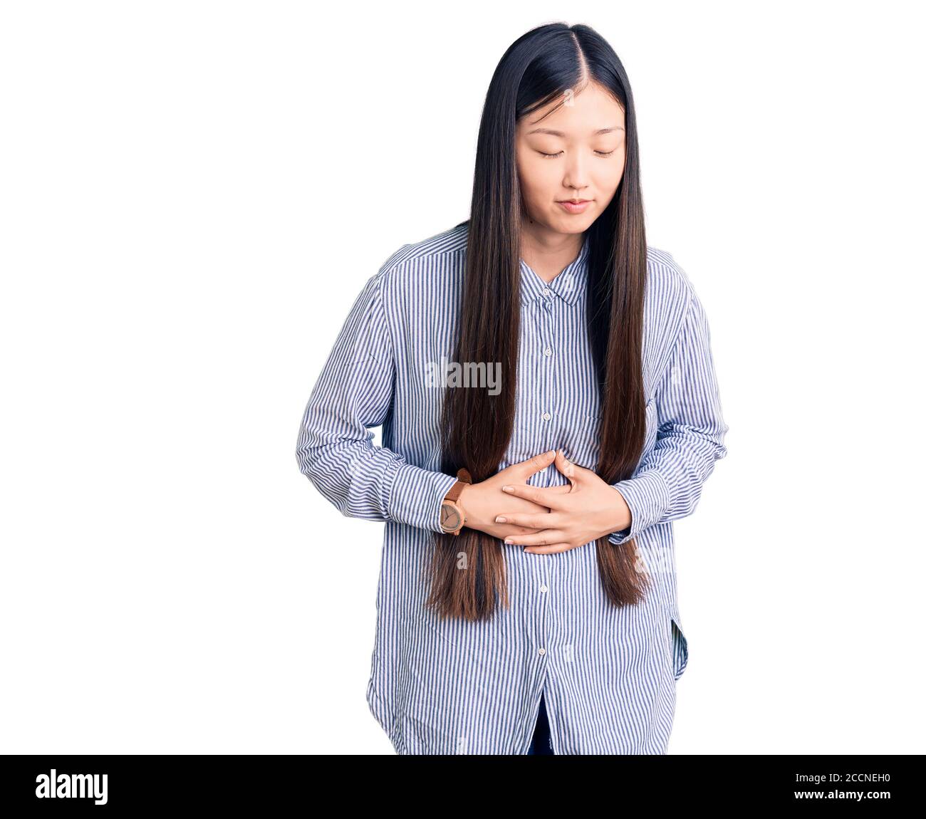 Young beautiful chinese woman wearing casual shirt with hand on stomach ...