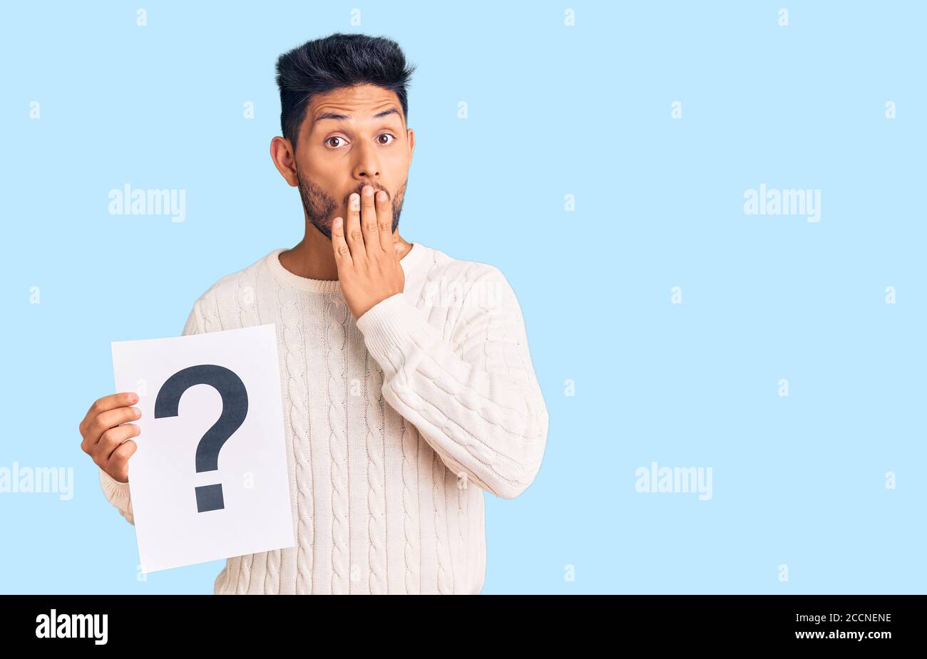 Handsome latin american young man holding question mark covering mouth ...