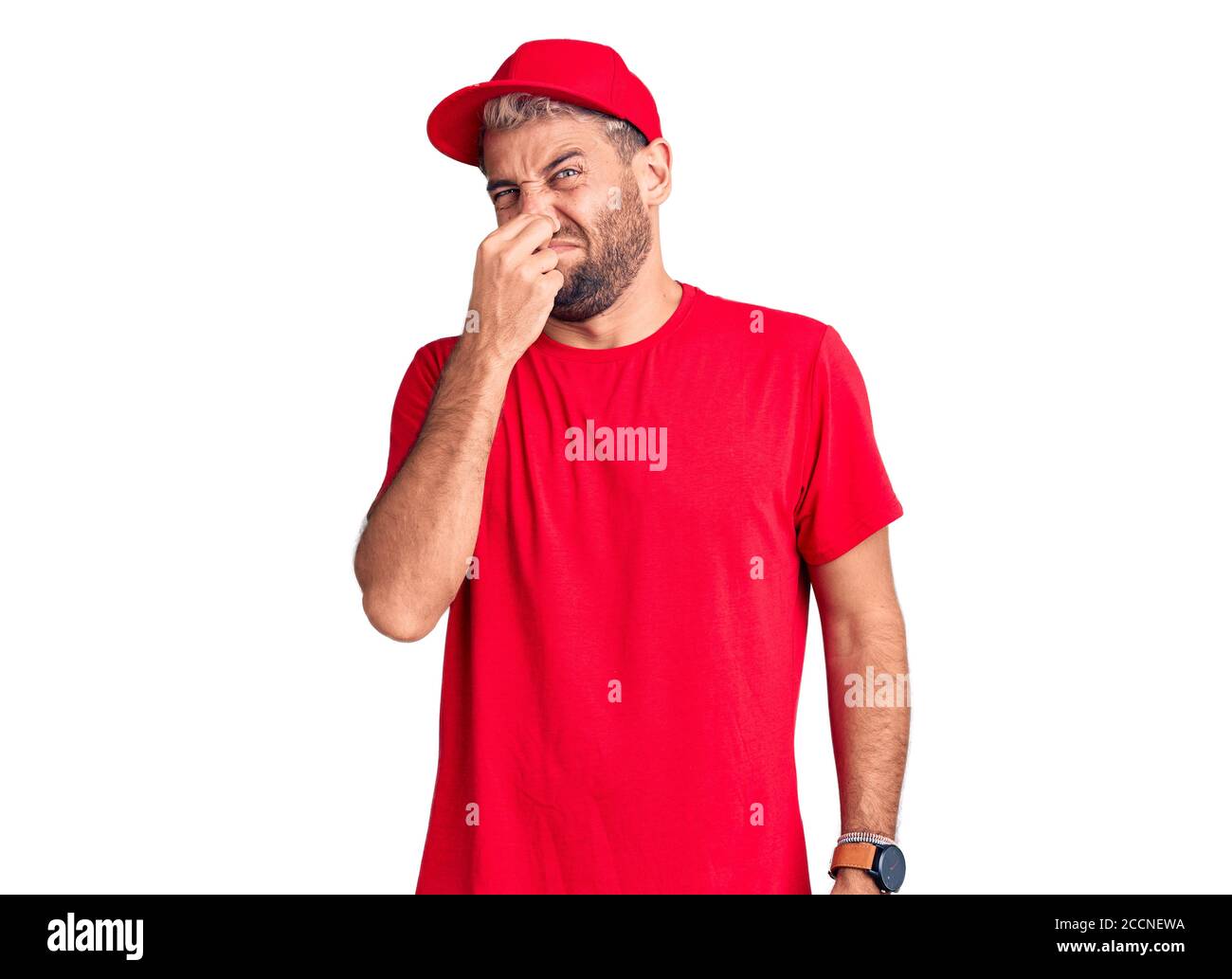 Young handsome blond man wearing t-shirt and cap smelling something ...