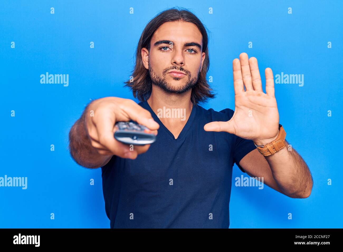 Young handsome man holding television remote control with open hand ...