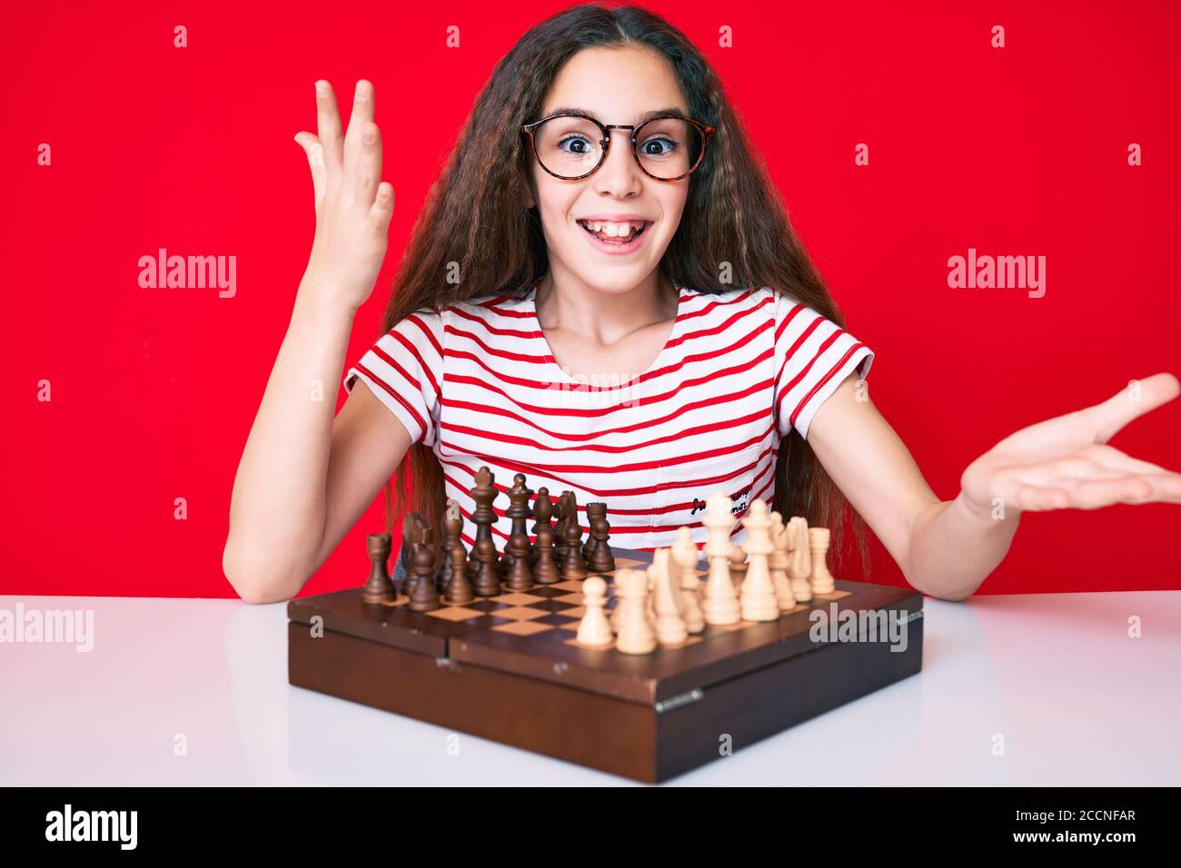Cute hispanic child girl playing chess celebrating achievement with ...