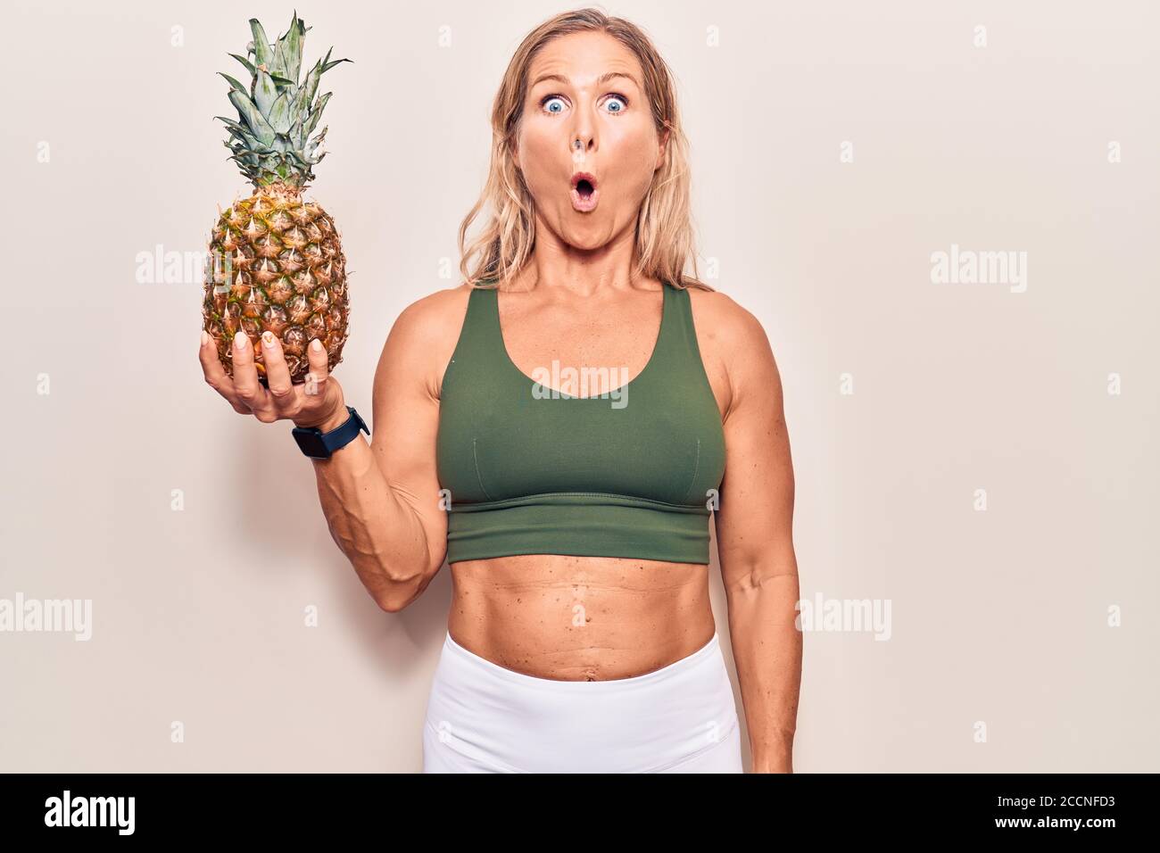 Middle age caucasian blonde woman holding pineapple scared and amazed ...