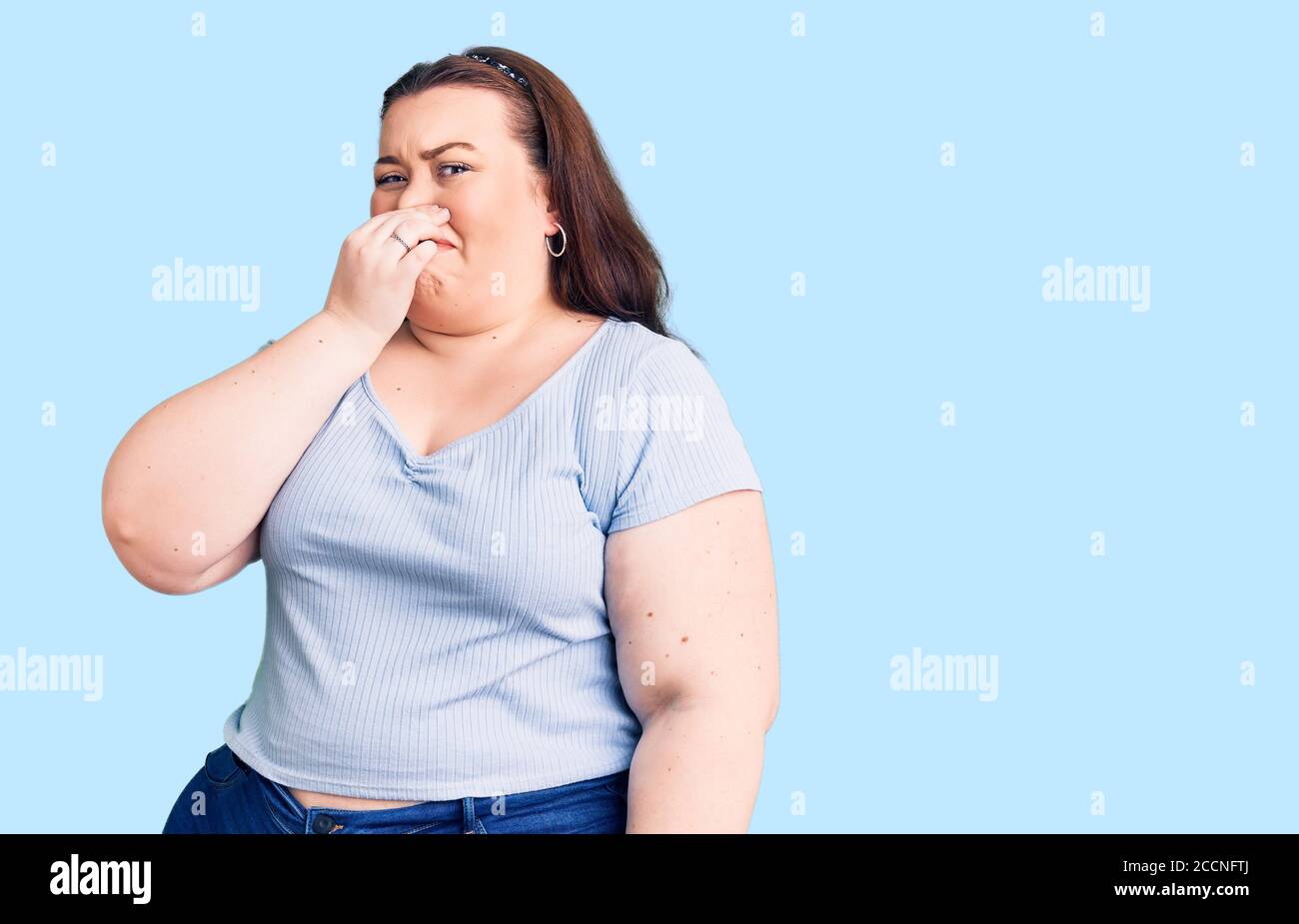 Young plus size woman wearing casual clothes smelling something stinky ...