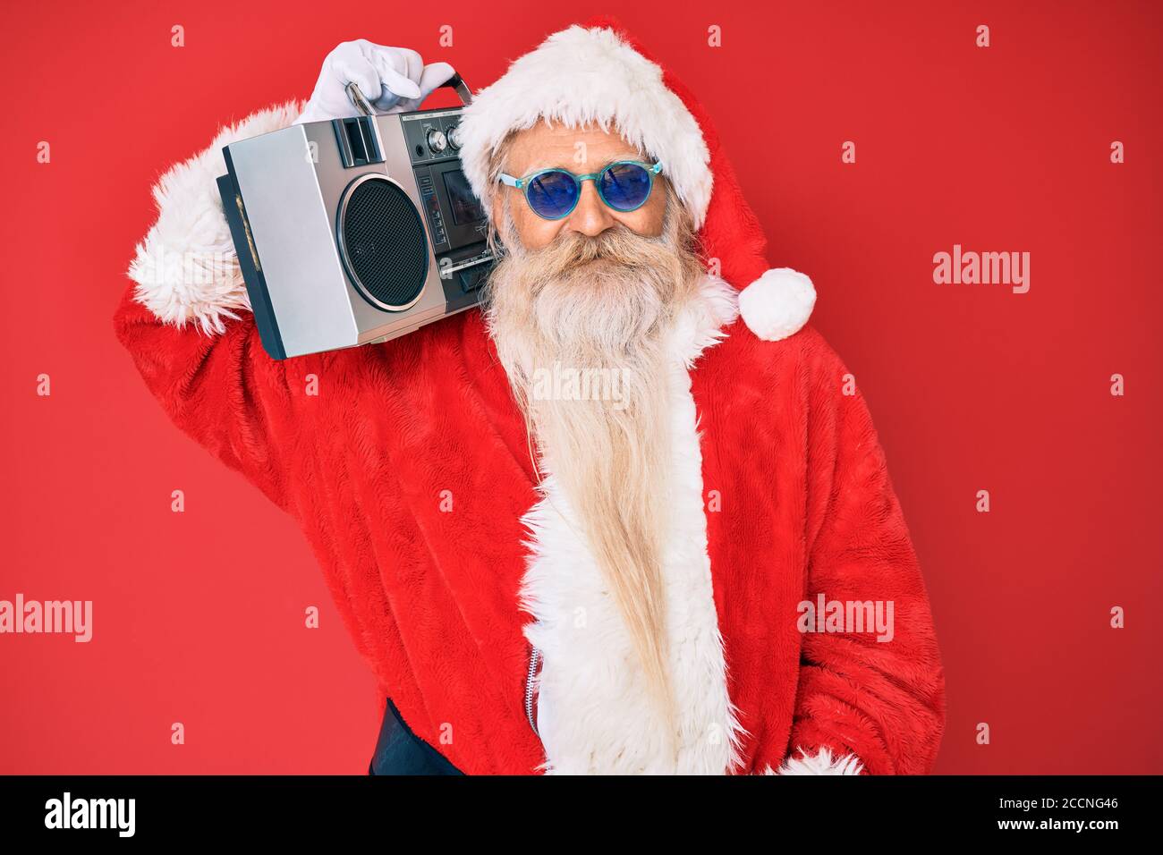 Old senior man wearing santa claus costume and boombox looking positive ...