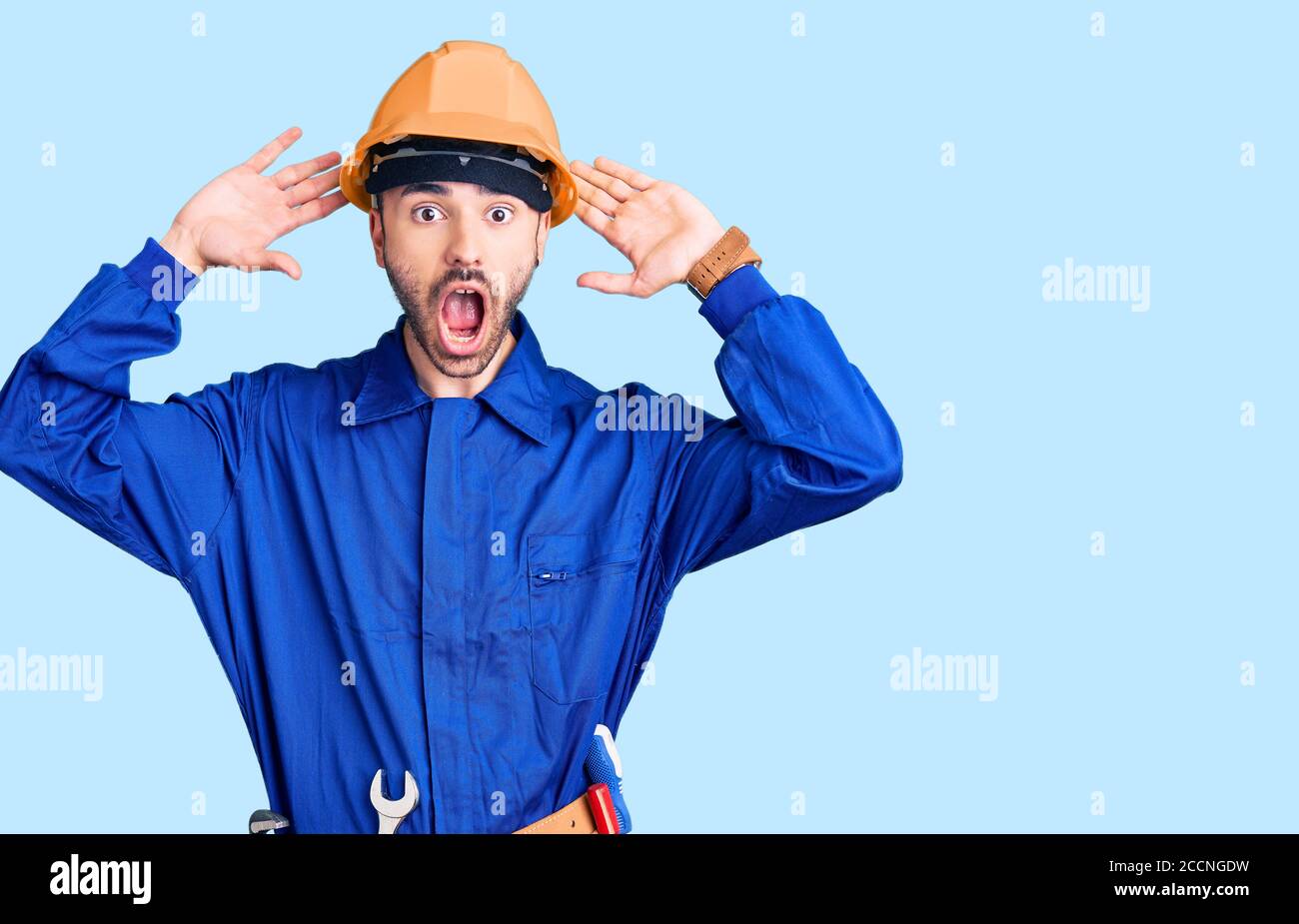 Young hispanic man wearing worker uniform crazy and scared with hands ...
