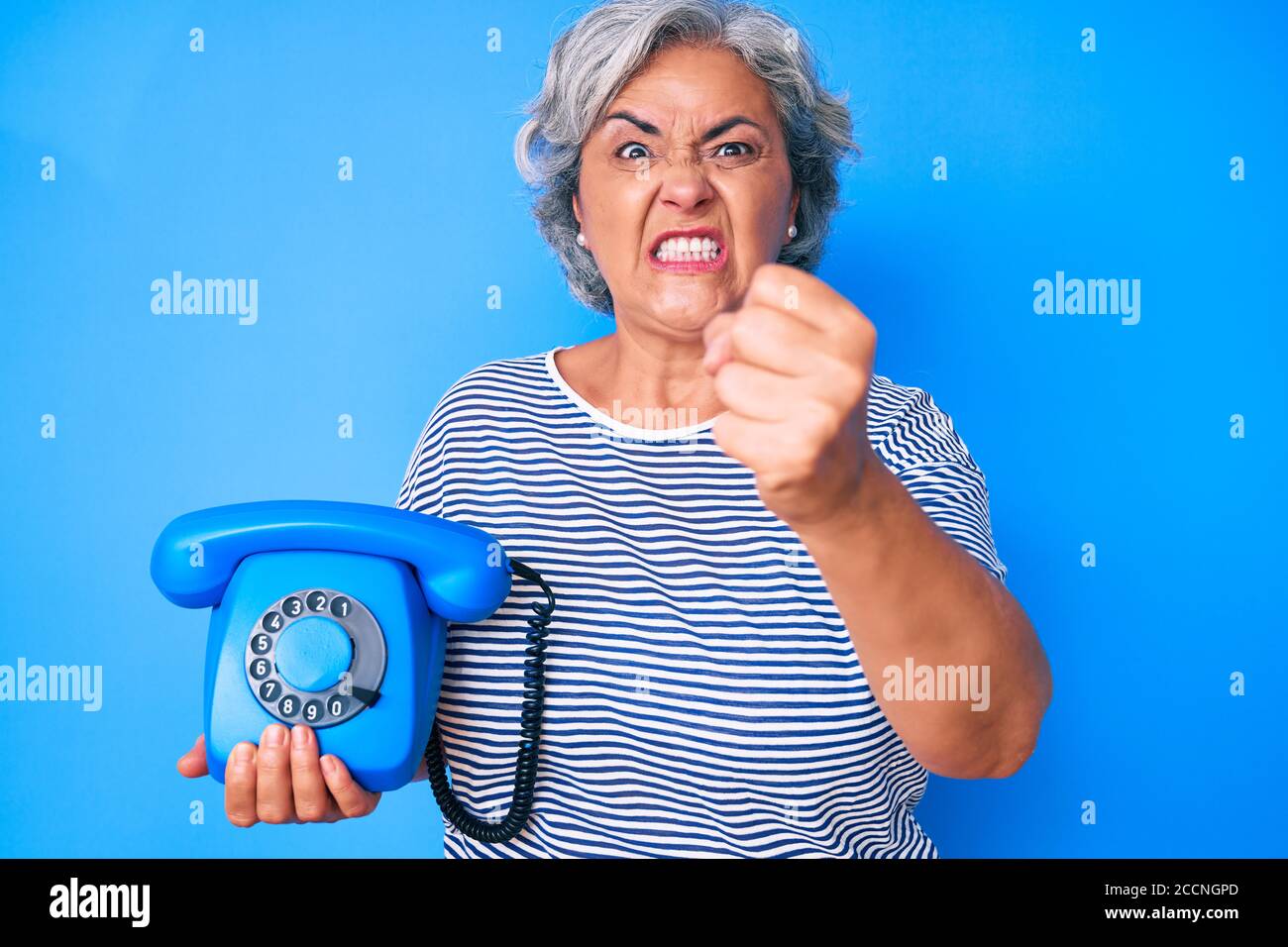 Senior hispanic grey- haired woman holding vintage telephone annoyed ...