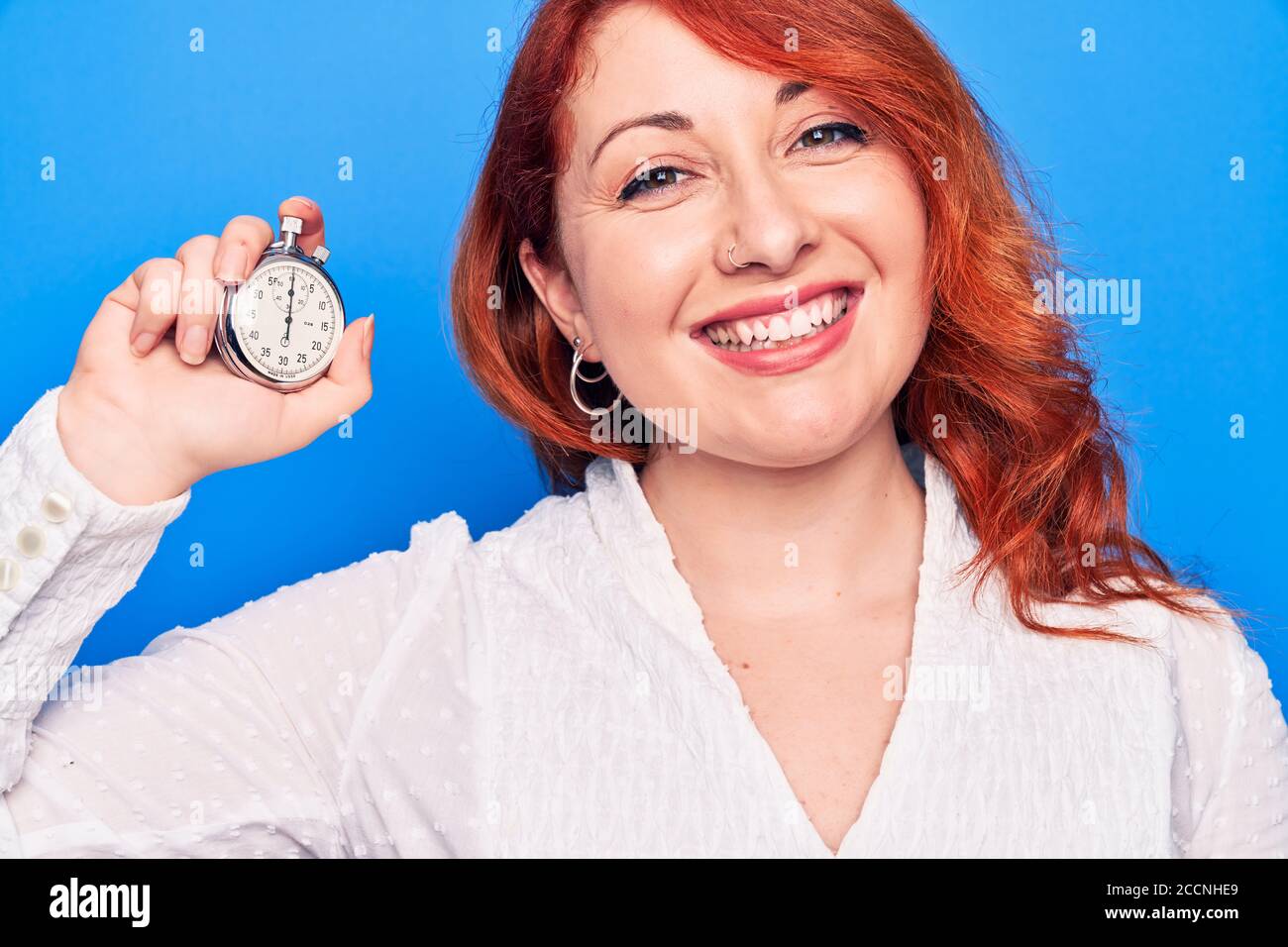 Young beautiful redhead woman doing countdown using stopwatch over blue ...