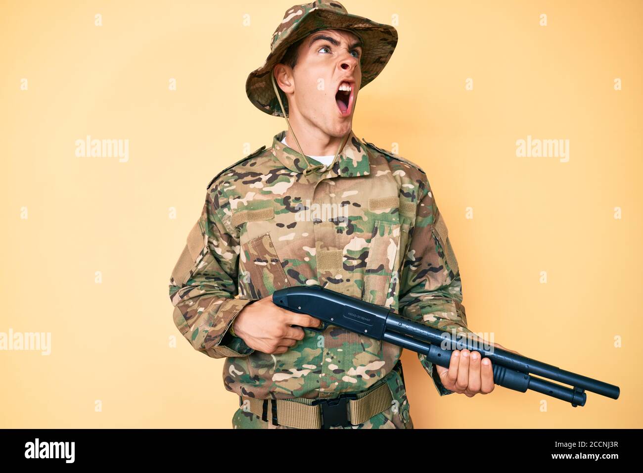 Young handsome man wearing camouflage army uniform holding shotgun ...