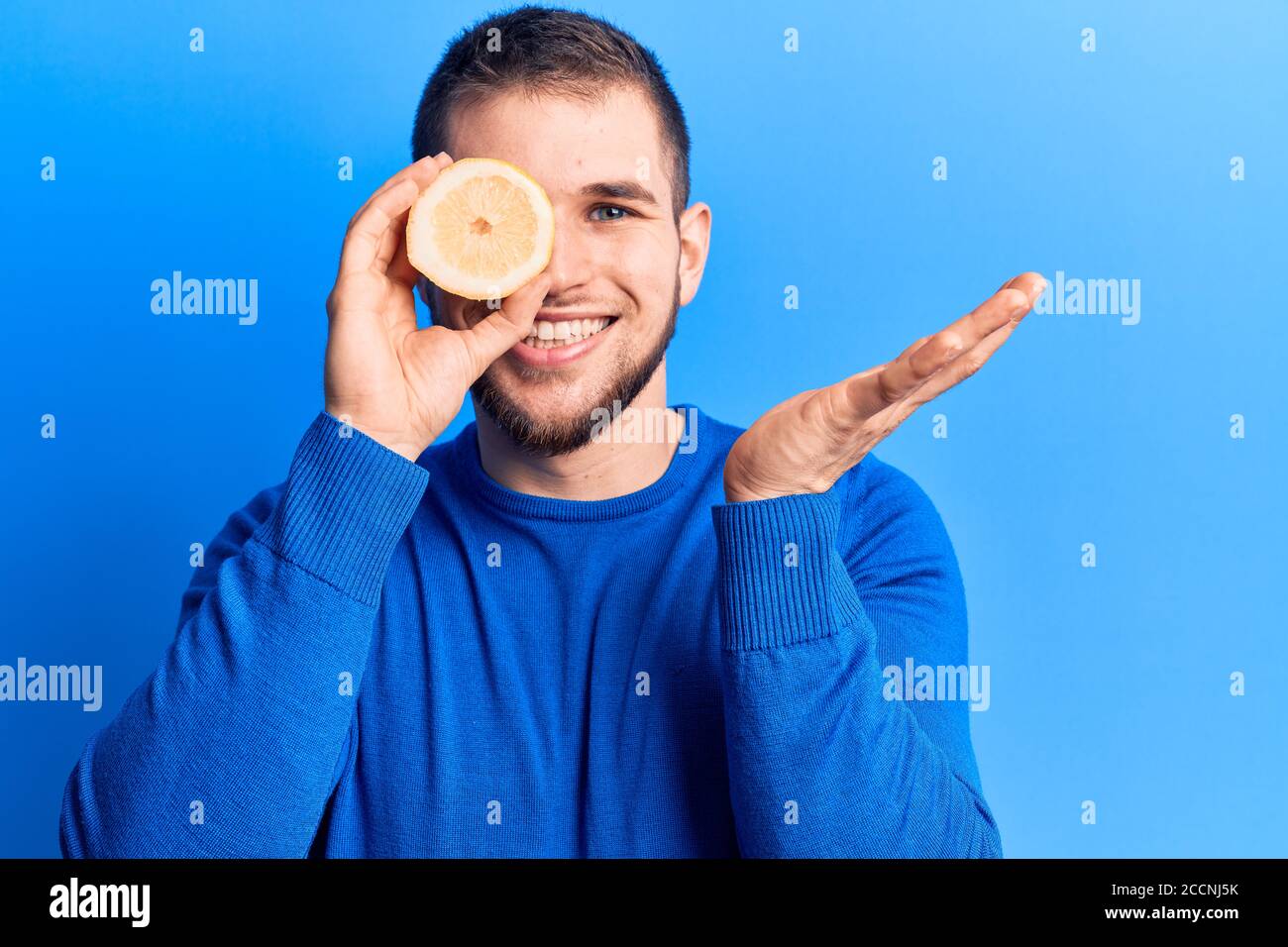 Young handsome man holding slice of lemon over eye celebrating ...