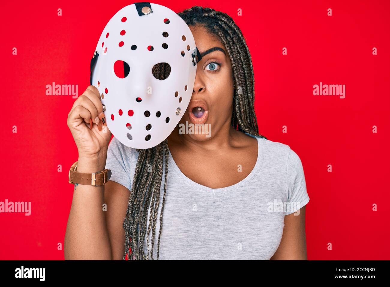 Young african american woman with braids wearing hockey mask scared and ...