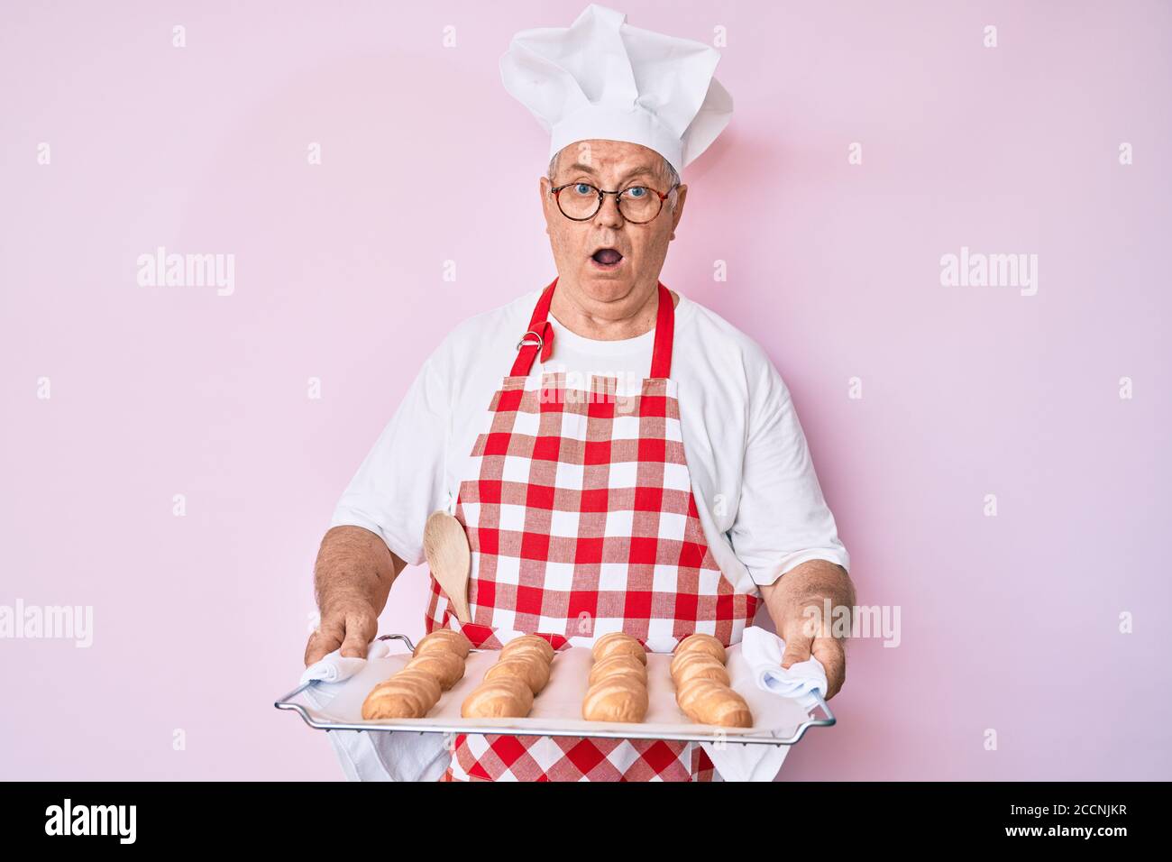 Senior grey-haired man wearing baker uniform holding homemade bread in ...