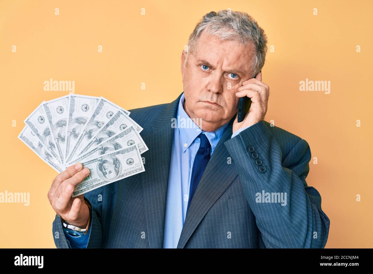 Senior grey-haired man wearing suit holding dollars and using ...
