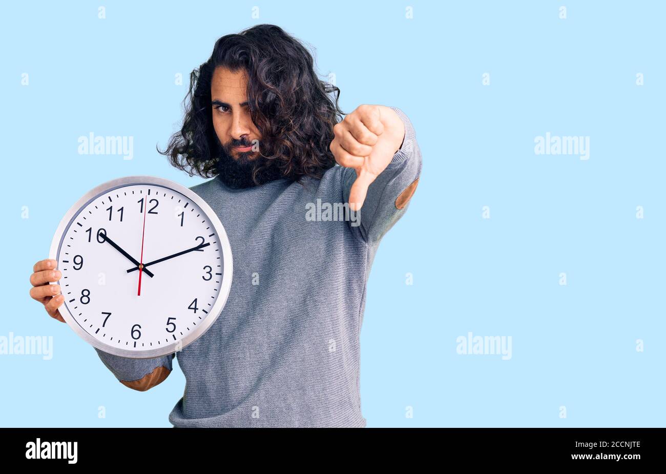 Young arab man holding big clock with angry face, negative sign showing ...