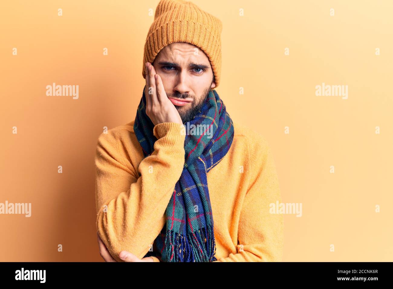 Young handsome man with beard wearing wool cap and scarf thinking ...