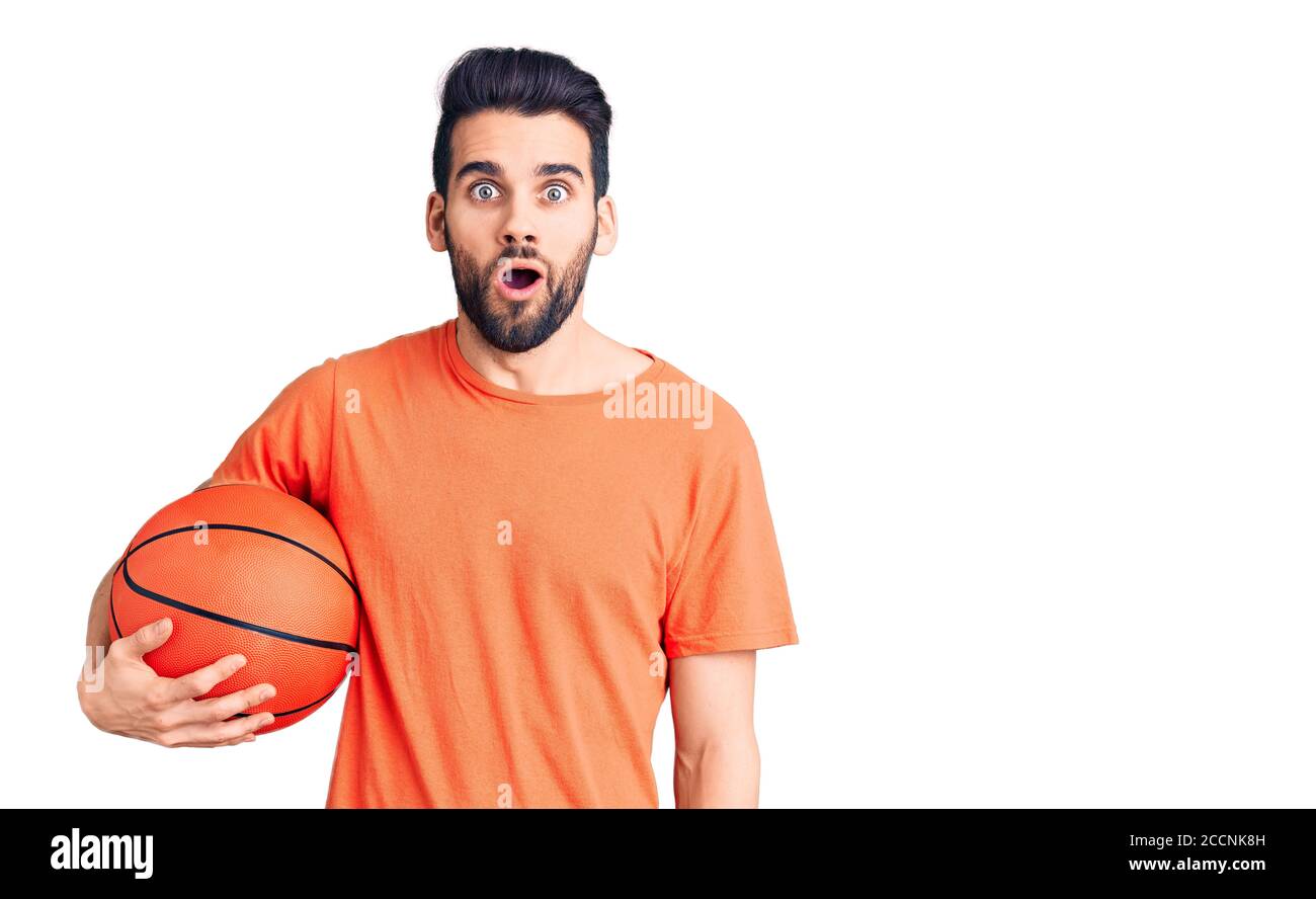 Young handsome man with beard hoilding basketball ball scared and ...