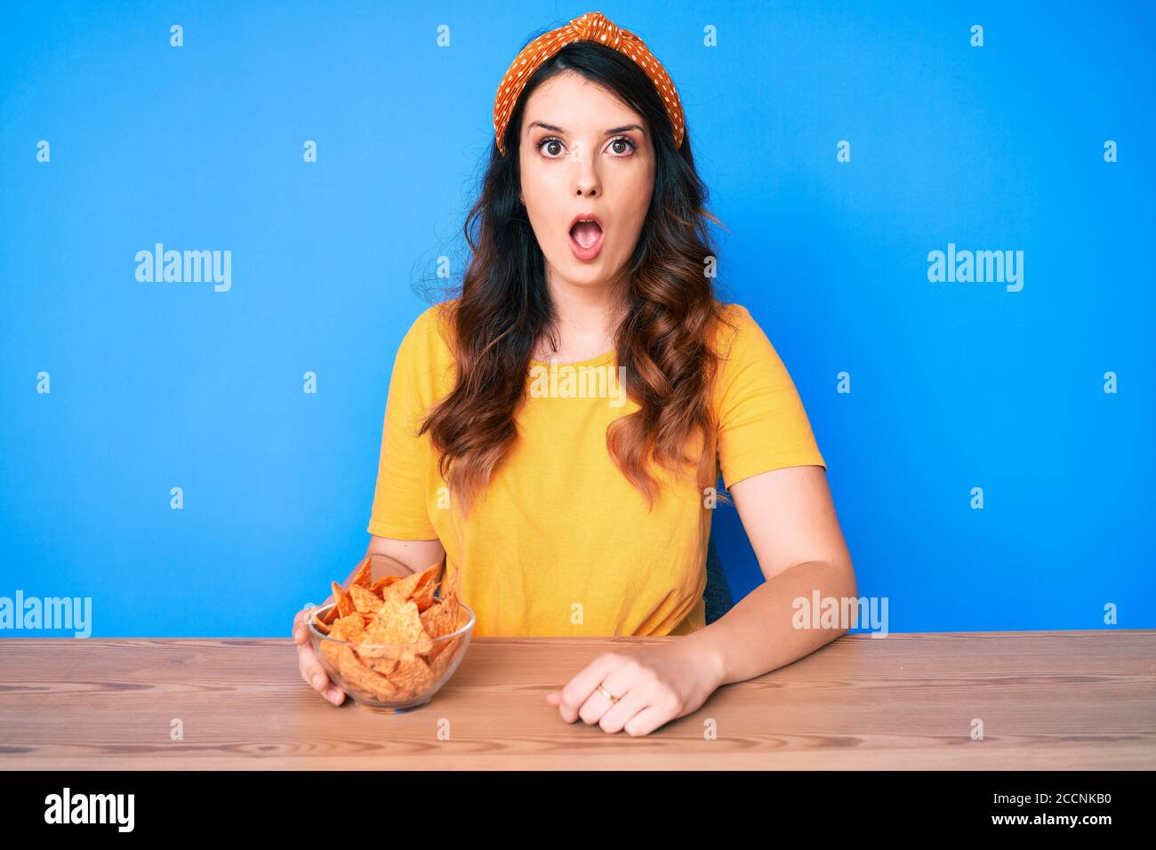 Young beautiful brunette woman sitting on the table eating nachos ...