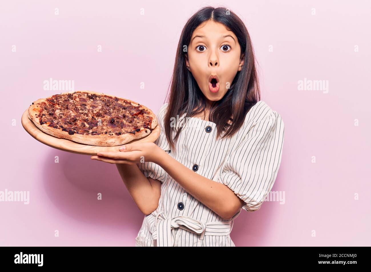 Beautiful child girl holding italian pizza scared and amazed with open ...