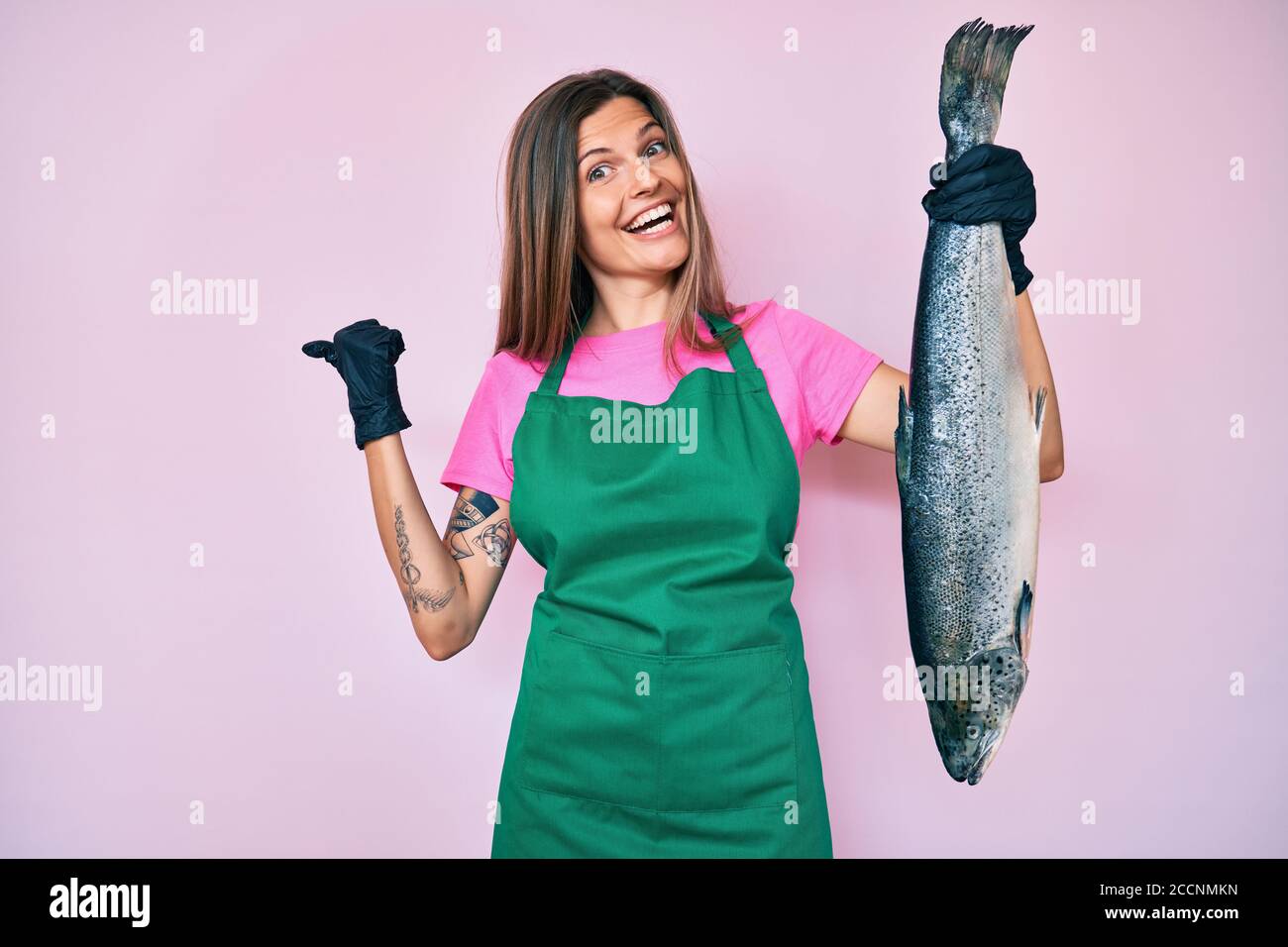 Beautiful caucasian woman fishmonger selling fresh raw salmon pointing ...