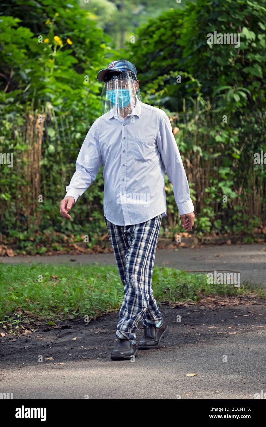 An Asian American man wearing both a surgical mask and a face shield ...
