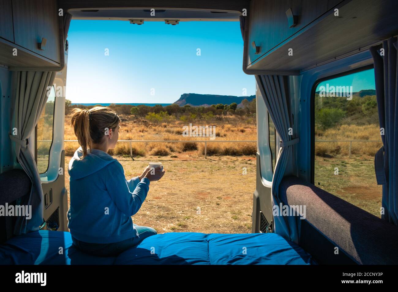 Holidays. Young woman having a coffee at the back side of a caravan ...