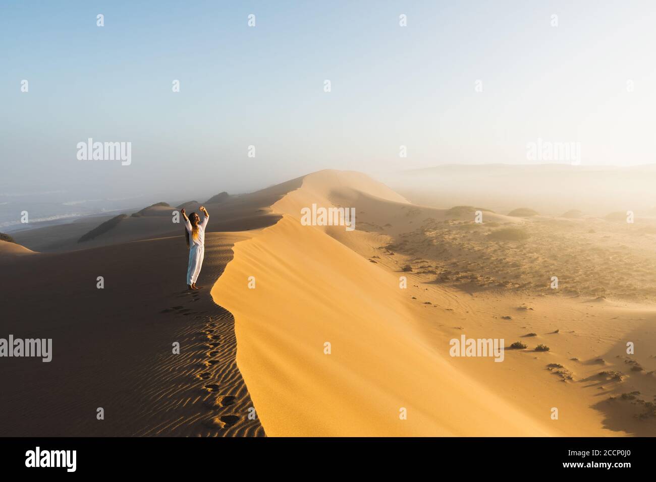 Woman enjoying sunrise on top of huge sand dune. Beautiful warm sun ...
