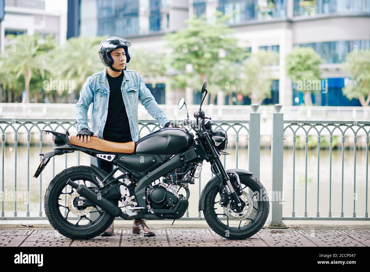 Serious handsome Asian man in helmet standing next to his motorcycle on ...