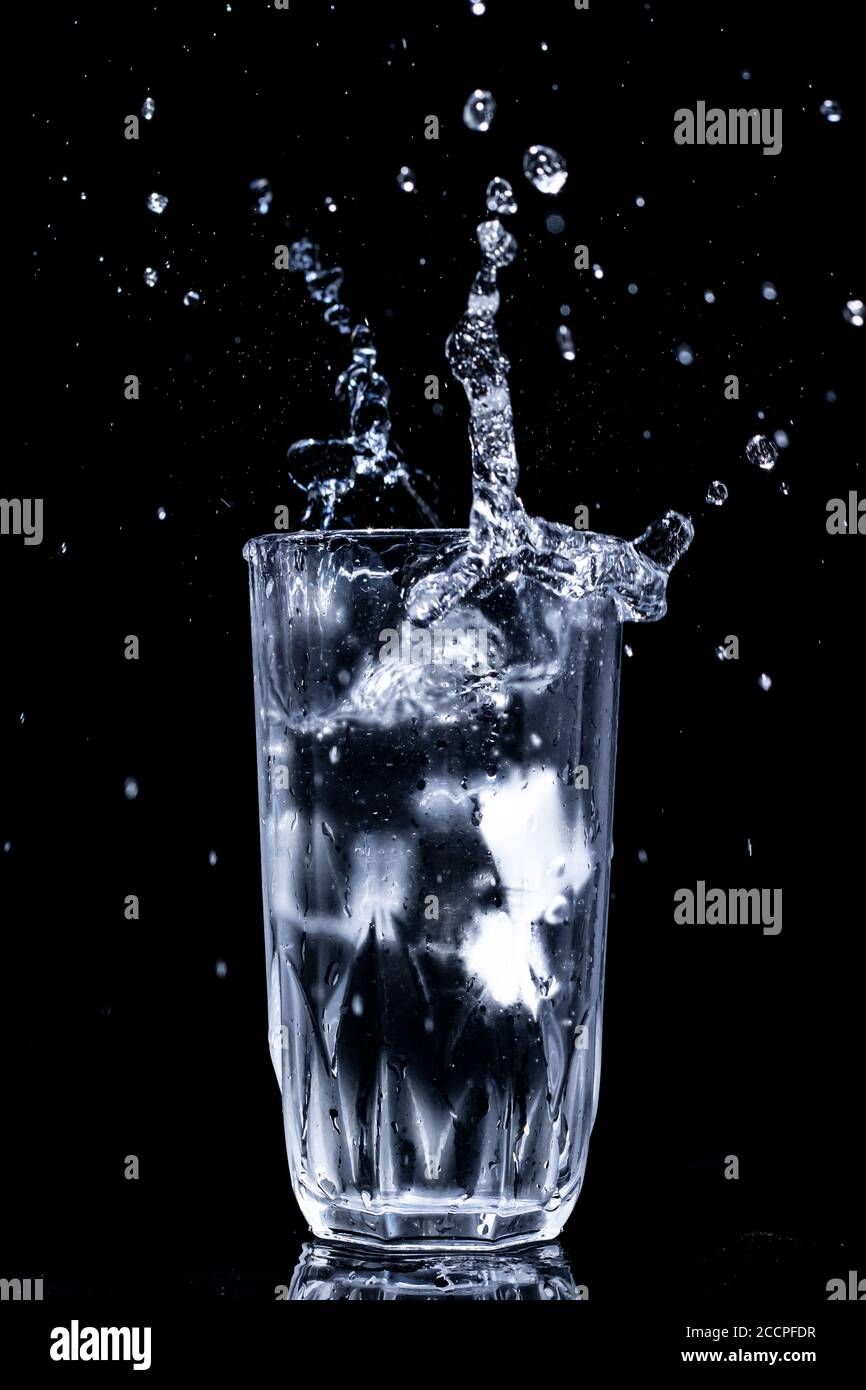 high speed photography of ice splashing in a glass of water on black ...