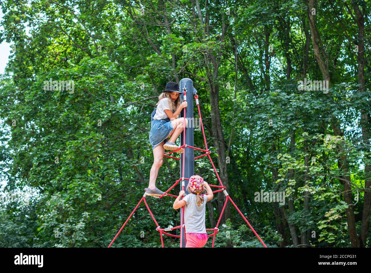 two girls climb up the rope pyramid in the park among the trees Stock ...