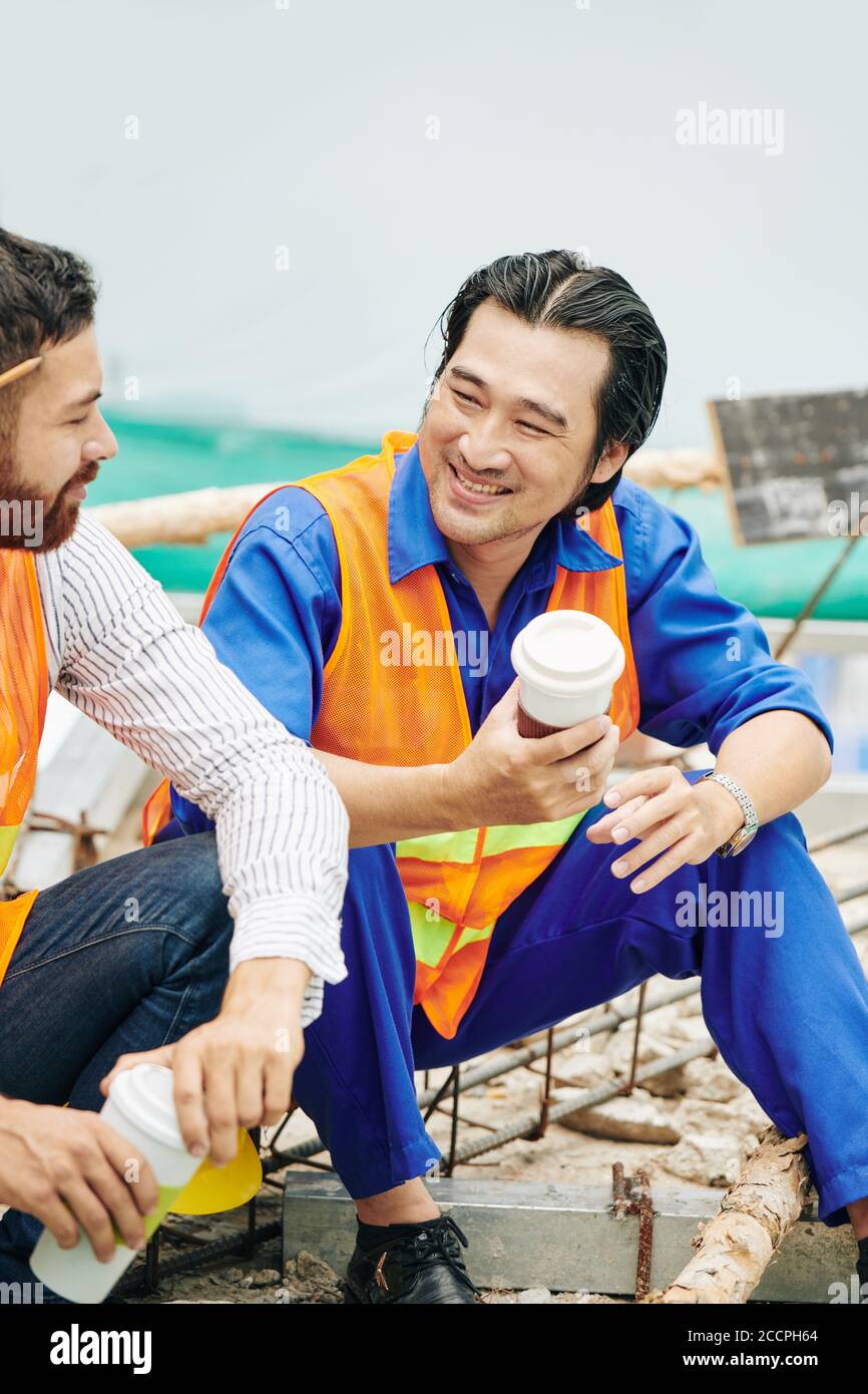 Handsome cheerful Vietnamese builder drinking coffee and talking to ...