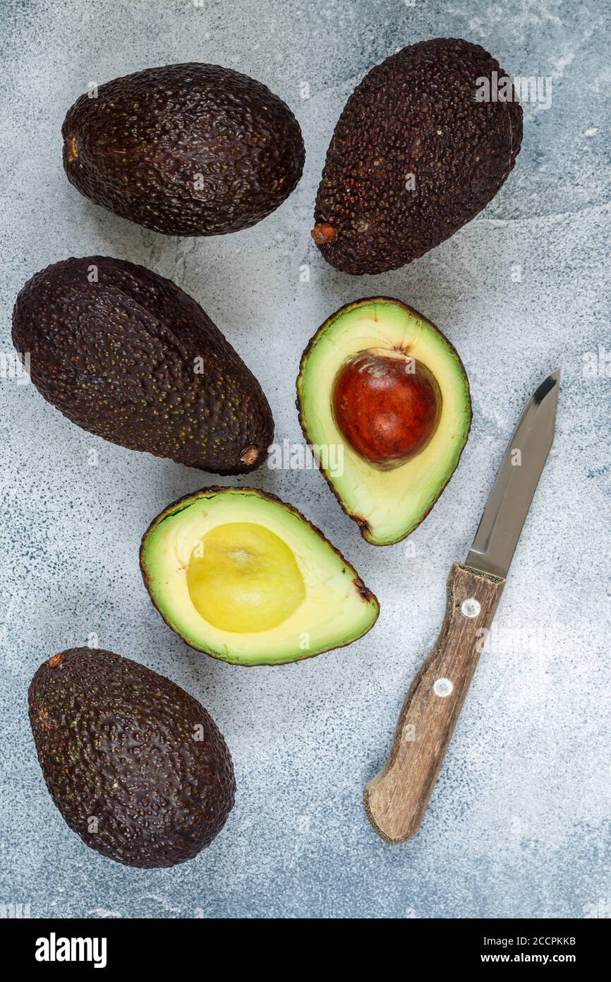 Whole and cut in half ripe organic avocados and a knife on a grey ...
